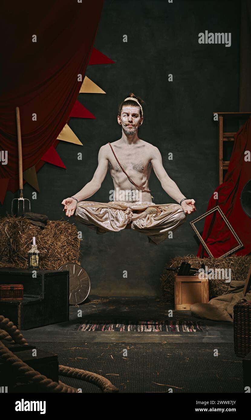 Pale man, yogi performing over dark retro circus backstage background ...