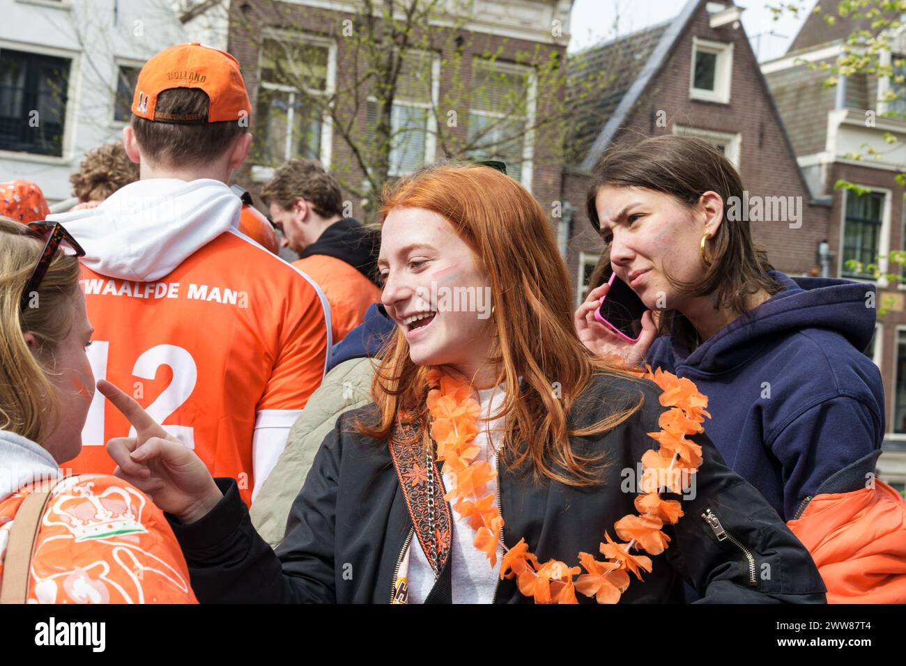 People in orange clothes are laughing and talking, holding drinks at an ...