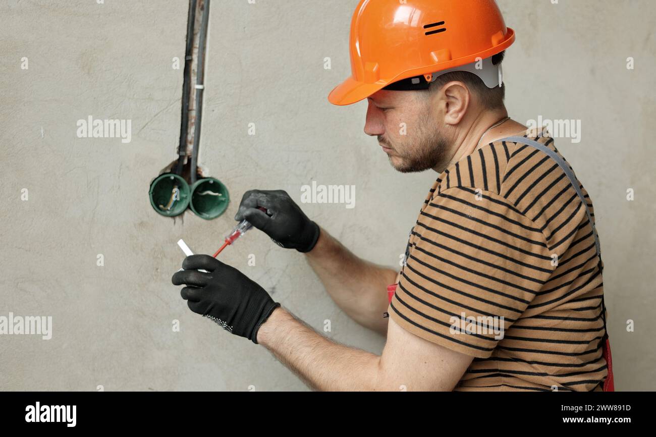 Electrician male in uniform, protective gloves and helmet checks ...
