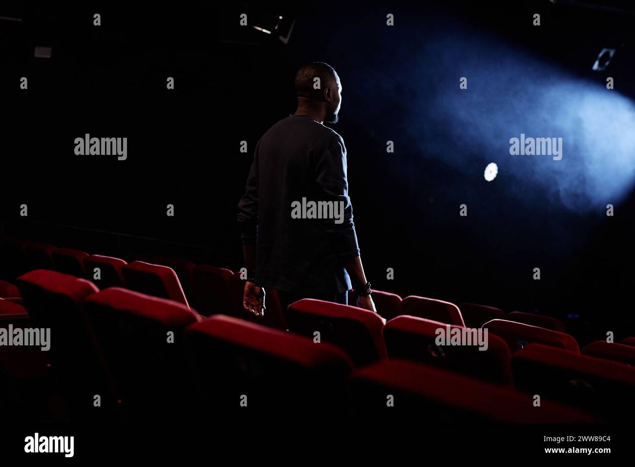 Dramatic back view of artist walking towards stage in empty theater ...