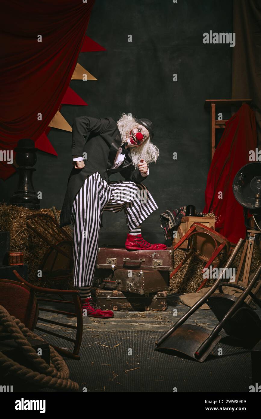 Clown emotional man in black hat, white face with red nose and striped ...