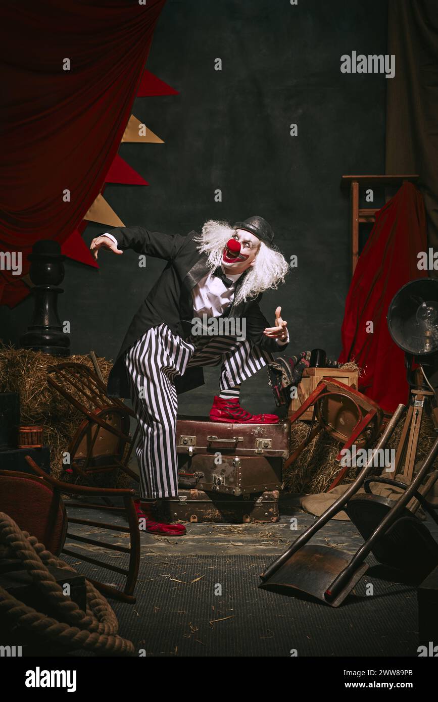 Clown in black hat, white face with red nose and striped pants playing ...