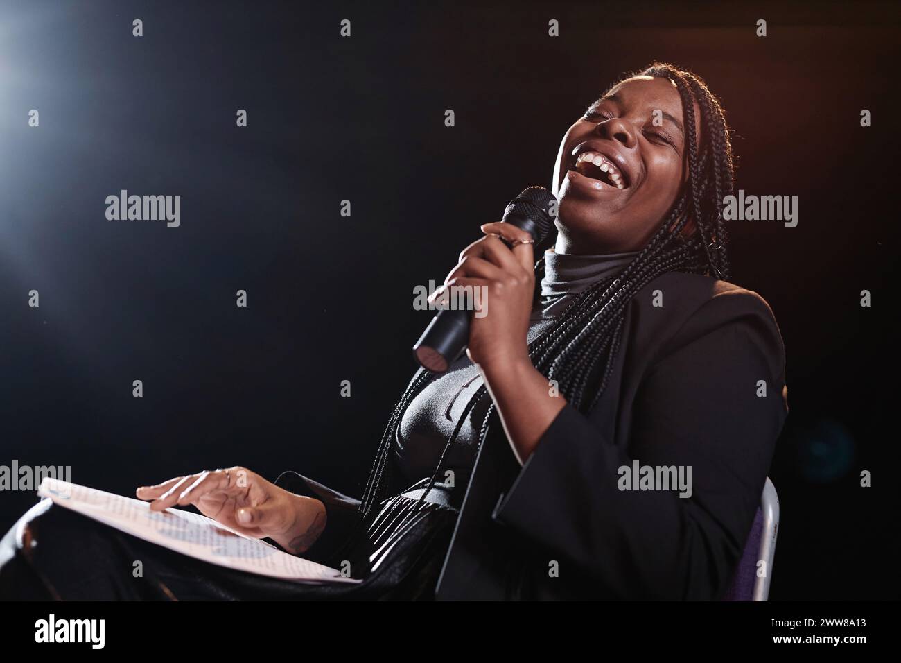 Portrait of Black woman laughing on stage and holding microphone while ...