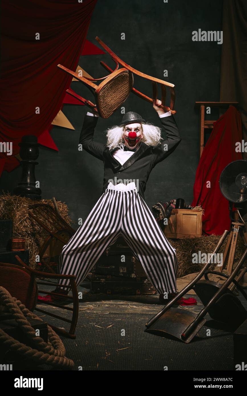Clown in black hat, white face with red nose and striped pants making ...