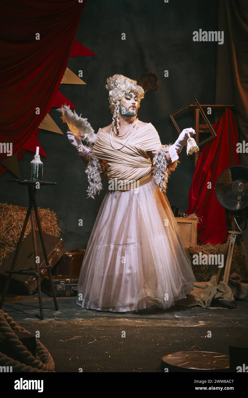 Drag queen in white dress and bright makeup over dark retro circus ...