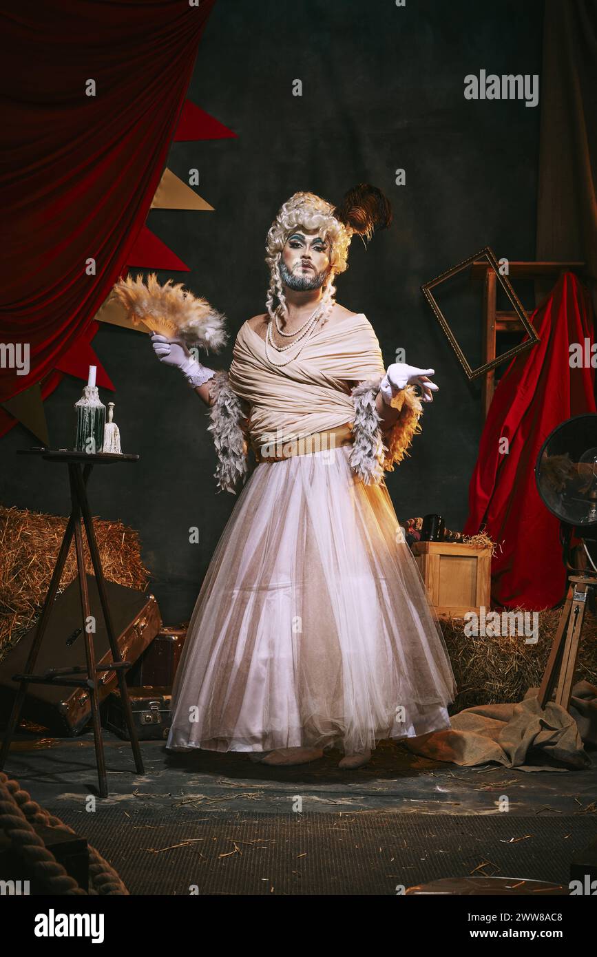 Drag queen, man in female white dress and bright makeup over dark retro ...