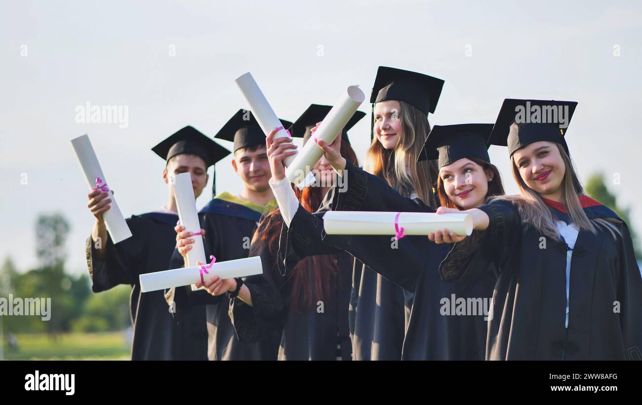 Cheerful graduates pose with raised diplomas on a sunny day Stock Photo ...