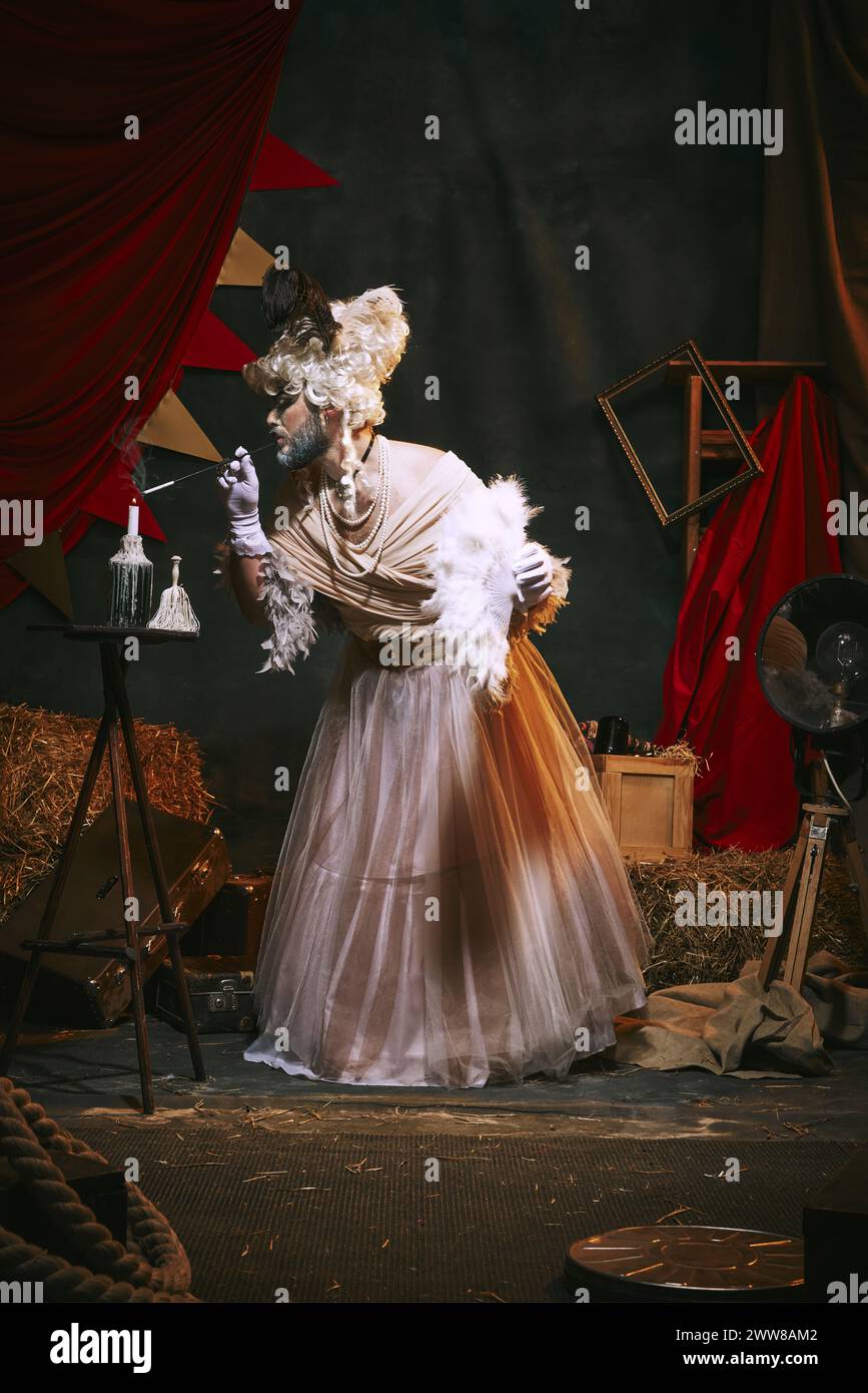 Drag queen in white dress and bright makeup smoking from candle over ...