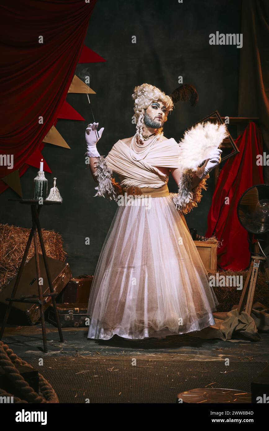 Drag queen in white dress and bright makeup over dark retro circus ...