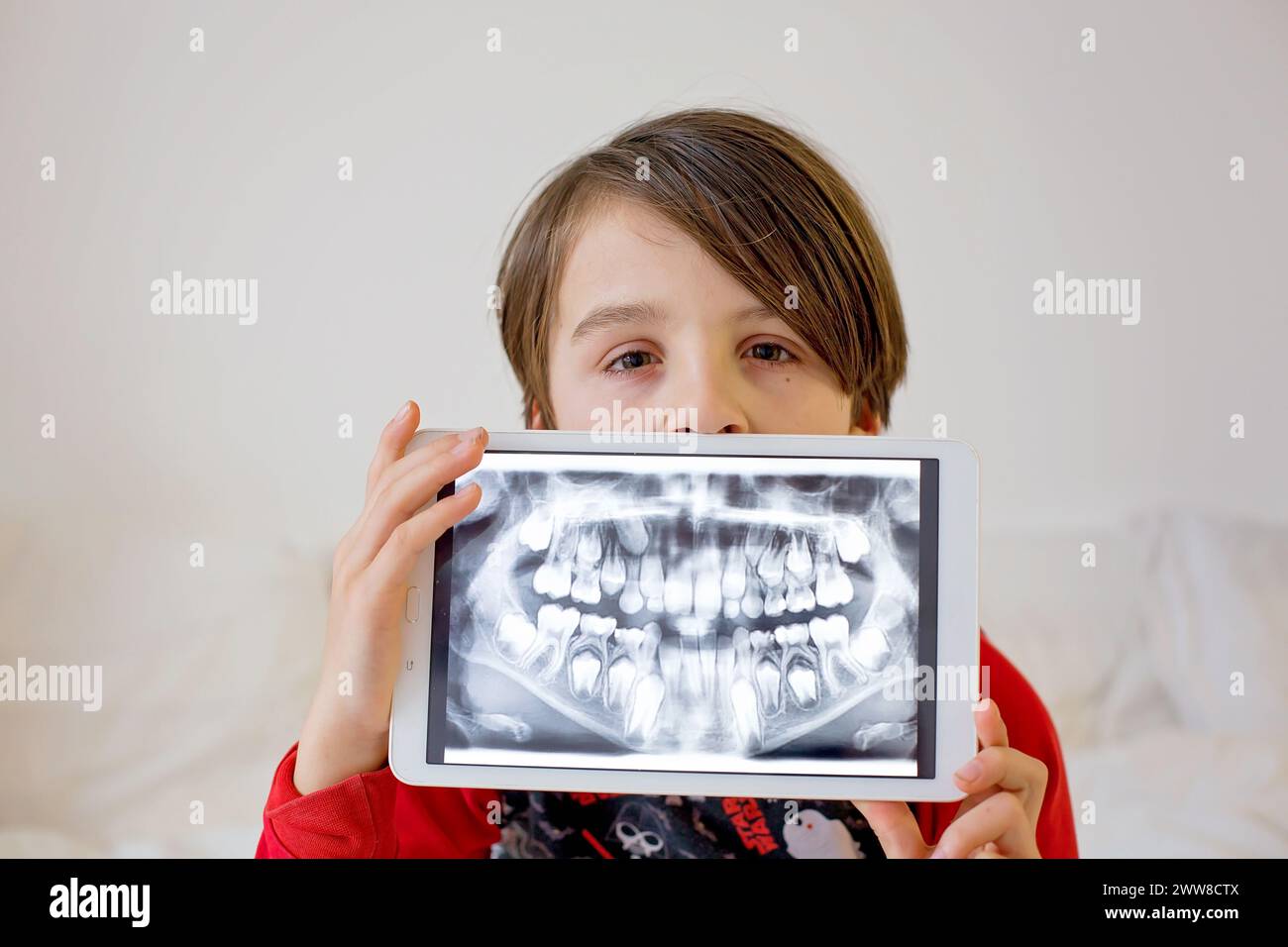 Child, preteen boy, holding tablet with a picture of his x-ray teeth ...