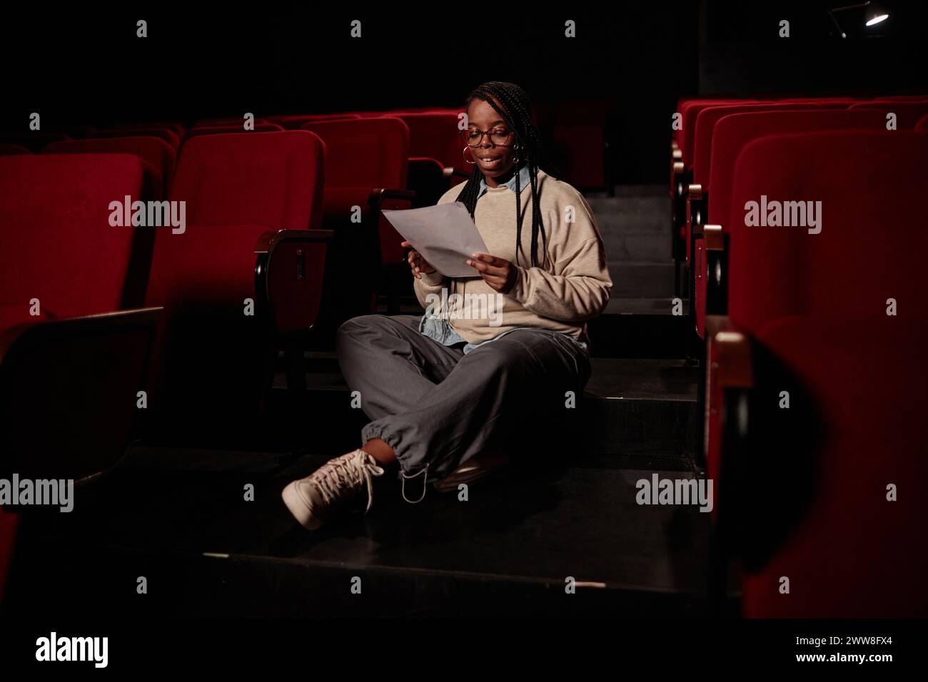 Full length portrait of Black female artist reading lines sitting on ...