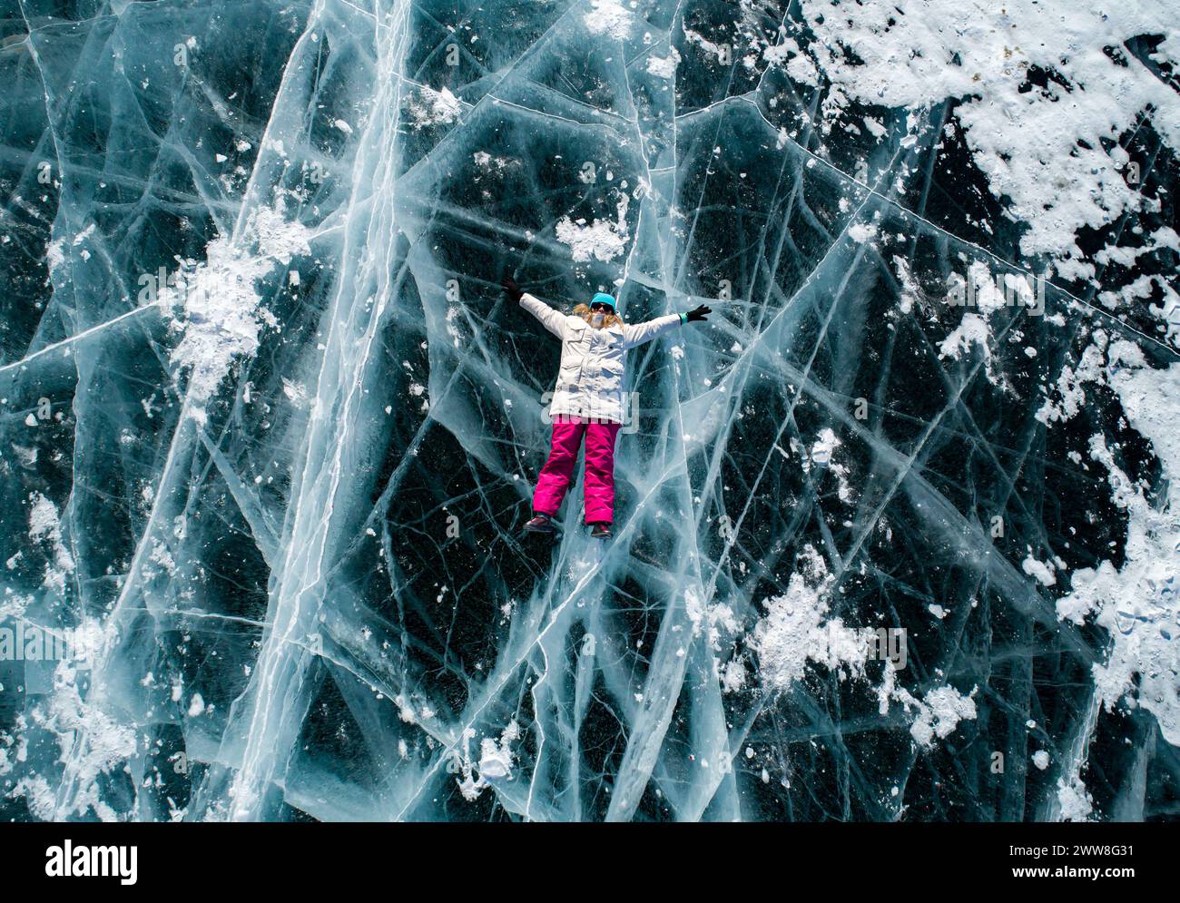Aerial top down shot of the young woman lying on the blue cracked ice ...