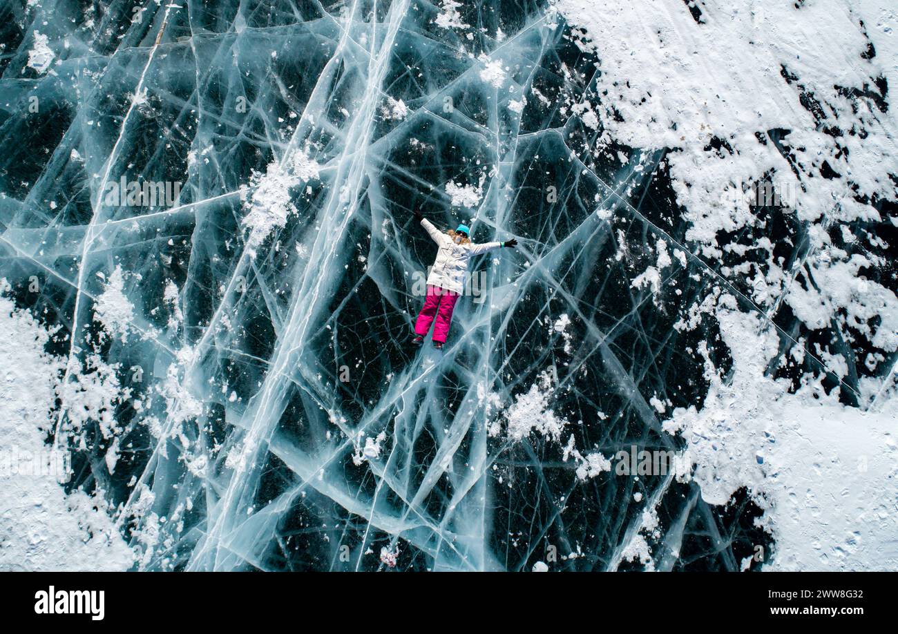 Aerial top down shot of the young woman lying on the blue cracked ice ...