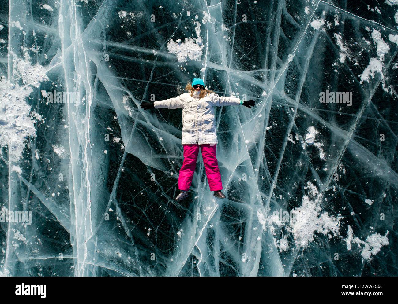 Aerial top down shot of the young woman lying on the blue cracked ice ...