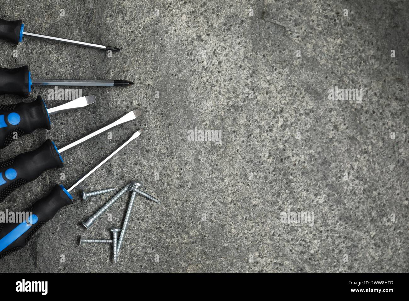 Set of screwdrivers and screws on grey table, top view. Space for text ...