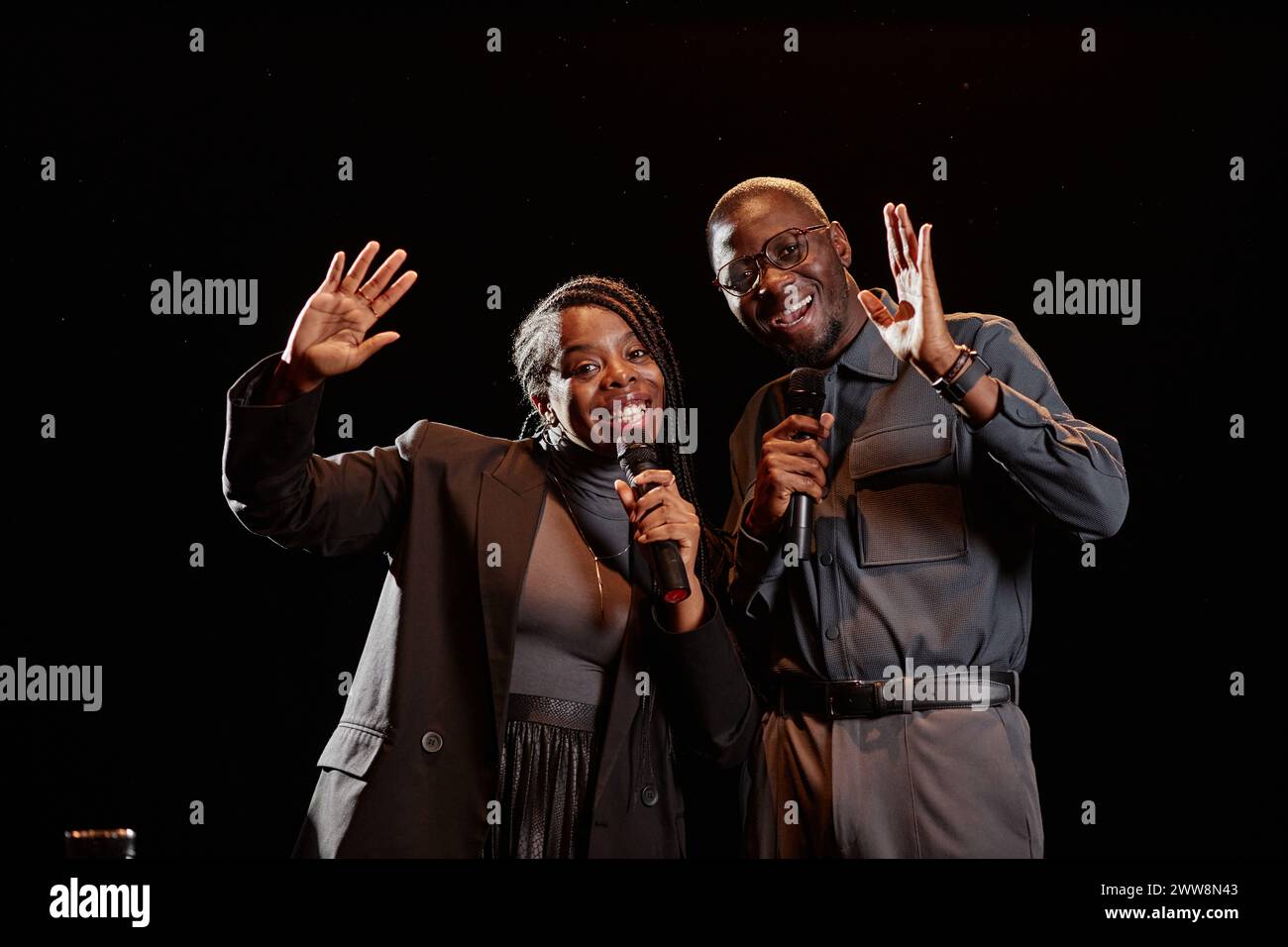 Portrait of two Black performers on stage speaking to microphone and ...