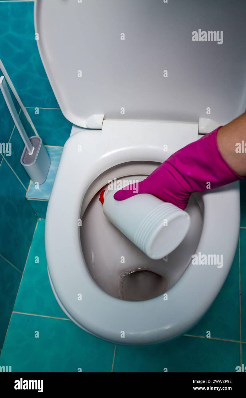 A hand wearing a pink glove carefully pours toilet cleaner from a ...