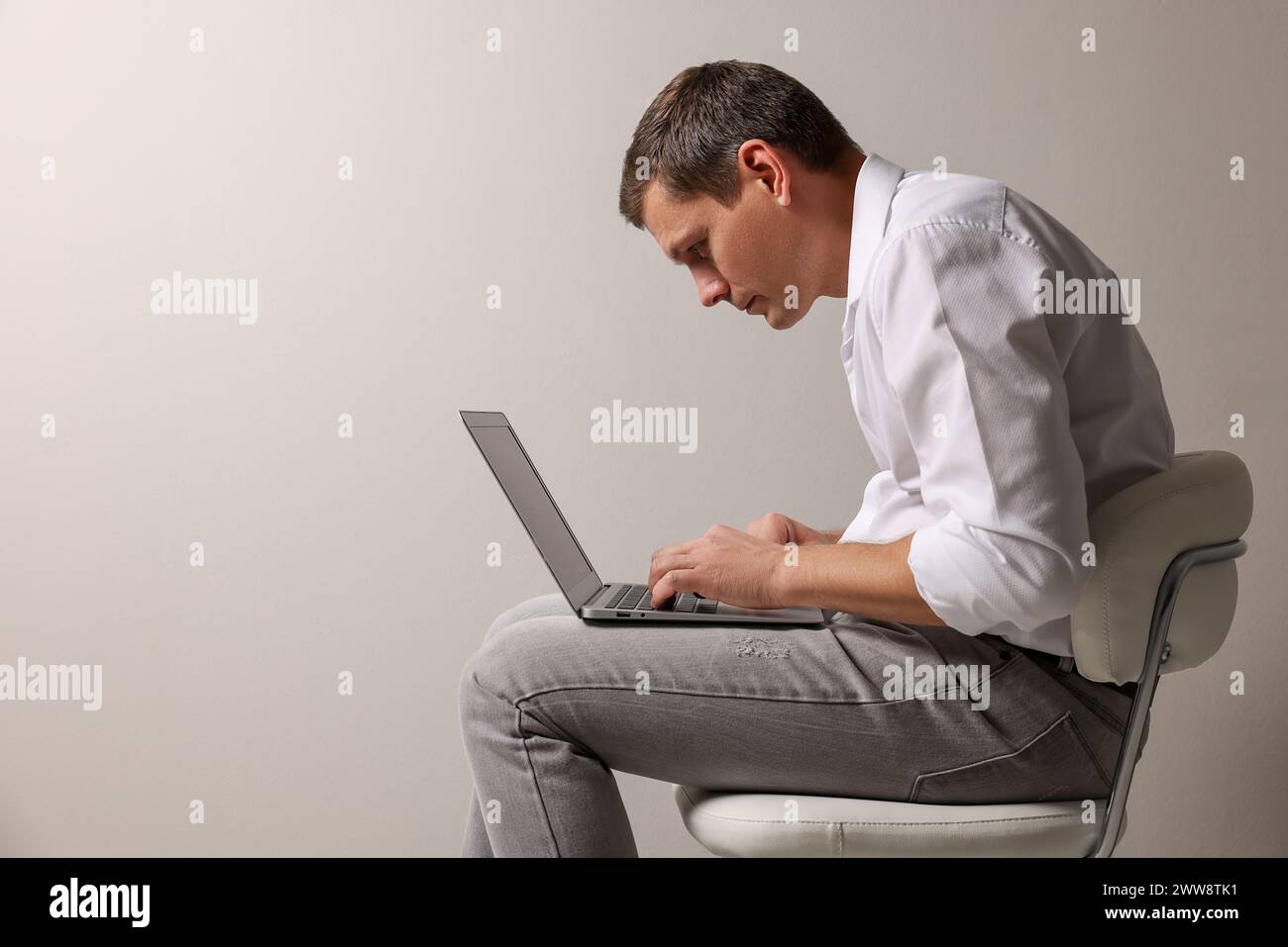 Man with bad posture using laptop while sitting on chair against grey ...