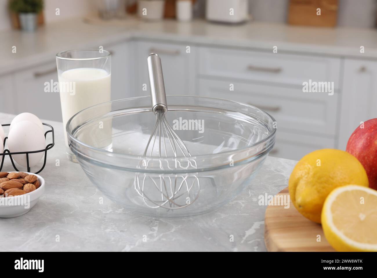 Metal whisk, bowl and different products on gray marble table in ...