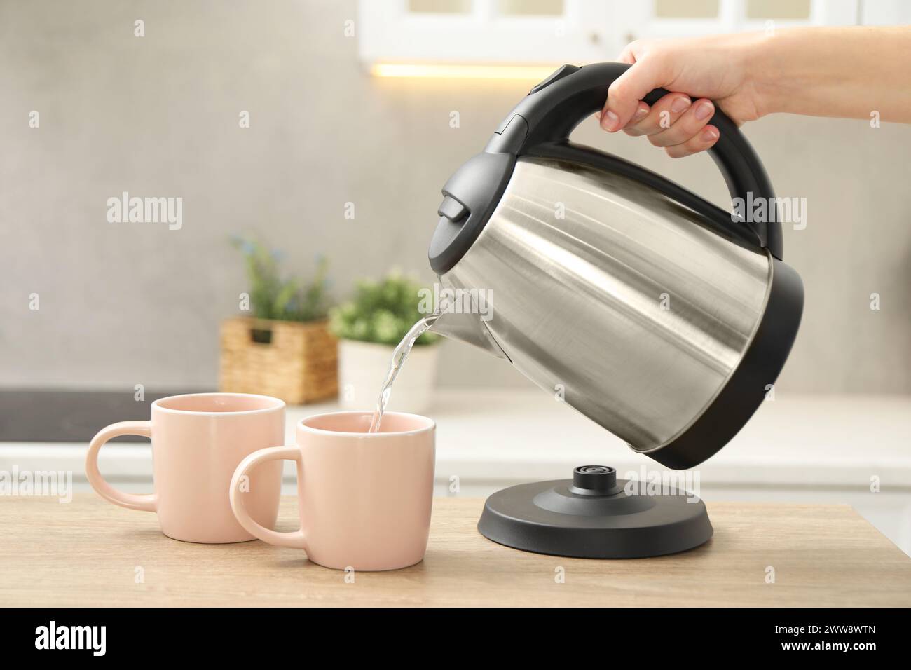 Woman pouring hot water from electric kettle into cup in kitchen ...