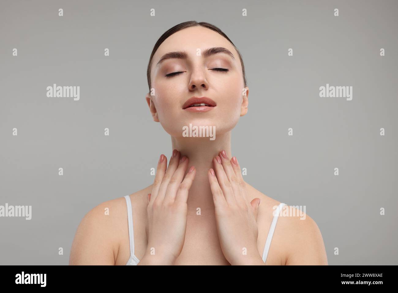 Beautiful woman touching her neck on grey background Stock Photo - Alamy