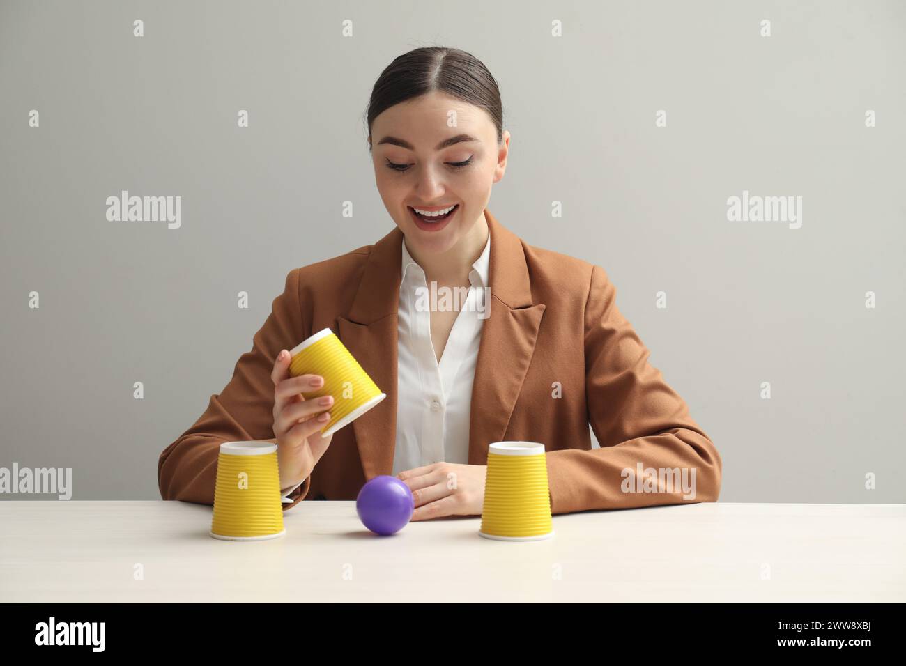 Shell game. Happy woman showing ball under cup at white table Stock ...