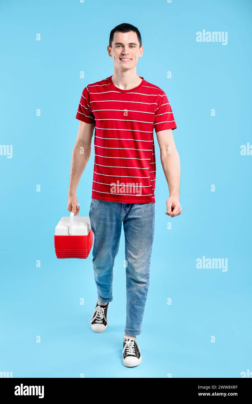 Man with cool box walking on light blue background Stock Photo - Alamy