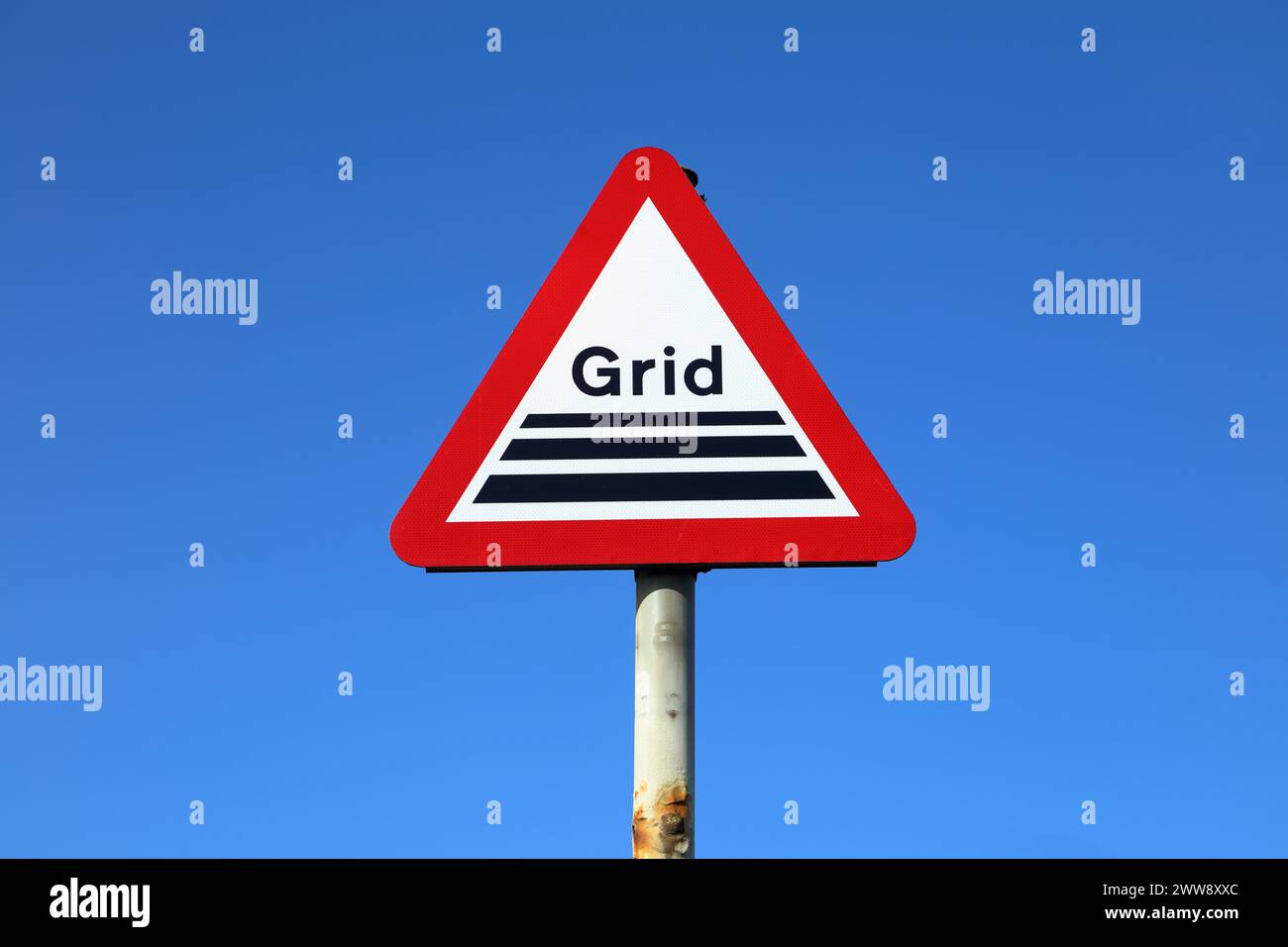 Warning sign mounted on a tall pole informing drivers of a cattle grid ...