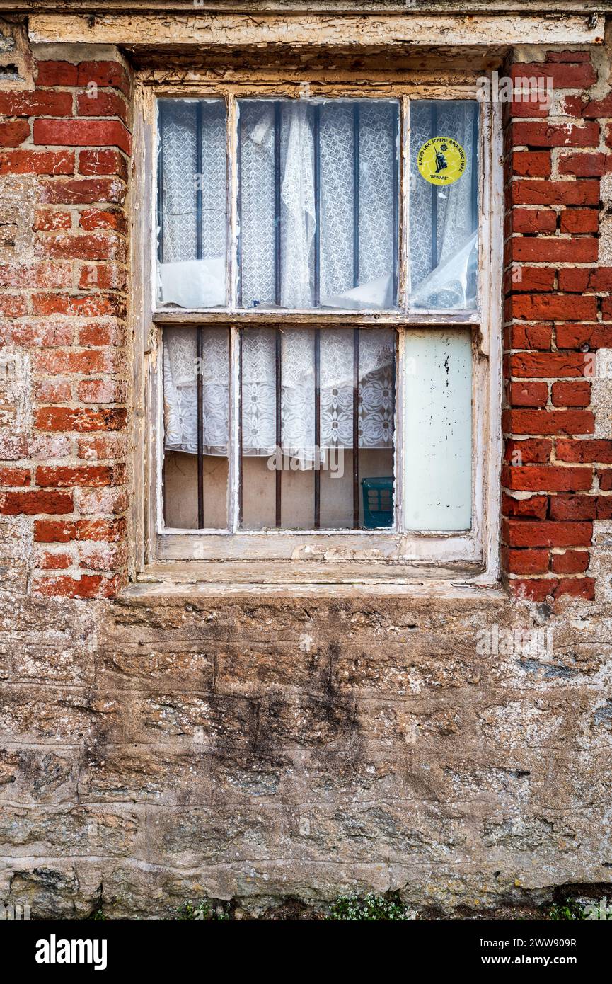 Atmospheric old derelict red brick shed with peeling paint door and windows on a grey sky day ...