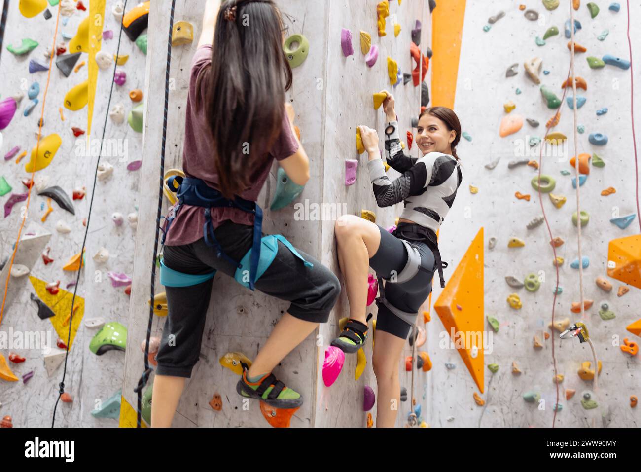 Two multiracial women doing rock climbing in the gym. Caucasian and ...