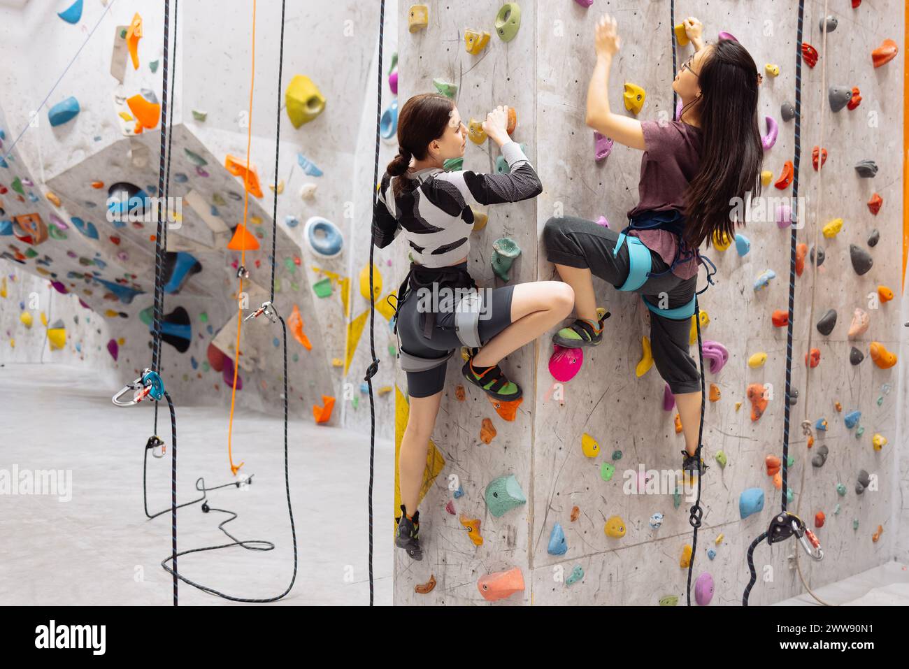 Two multiracial women doing rock climbing in the gym. Caucasian and ...