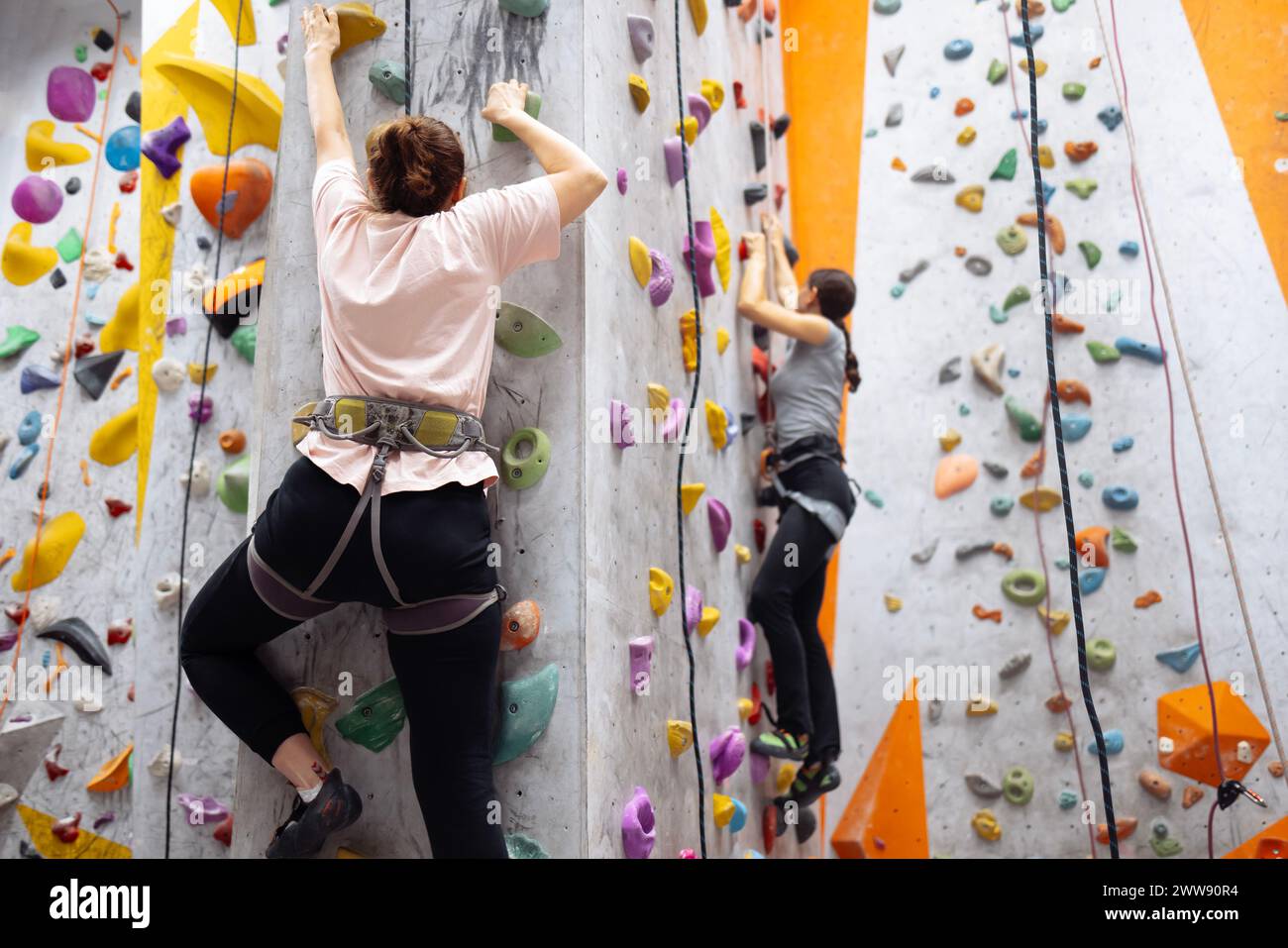 Two multiracial women doing rock climbing in the gym. Caucasian and ...