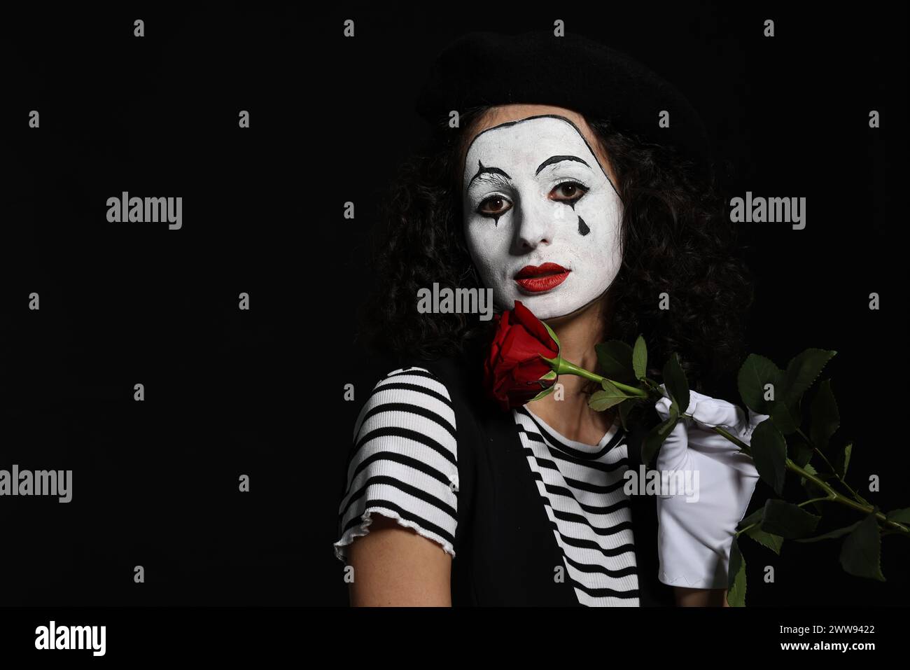 Young woman in mime costume with red rose posing on black background ...