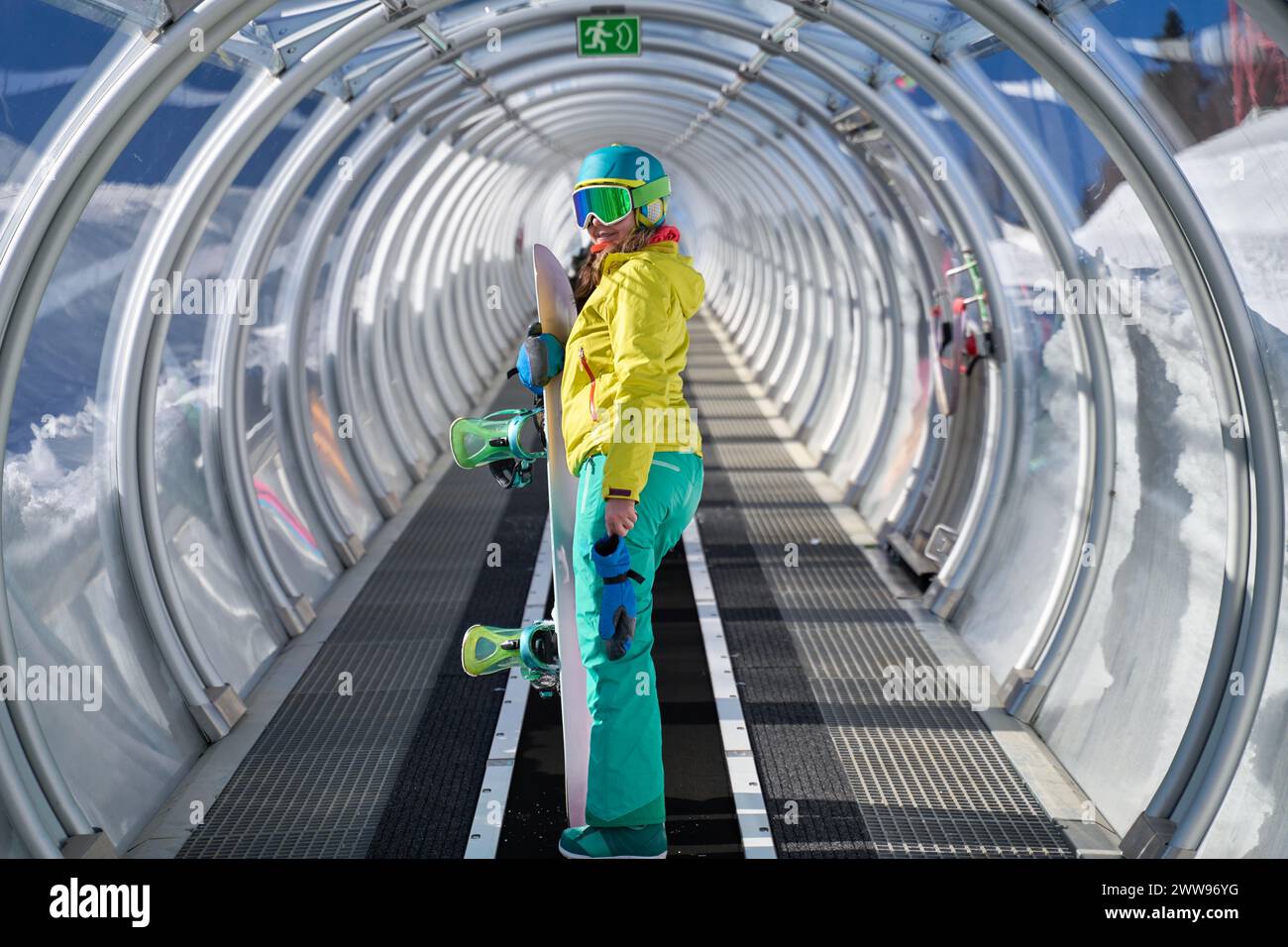 Rear view of a snowboarder with colorful gear in a transparent tunnel ...