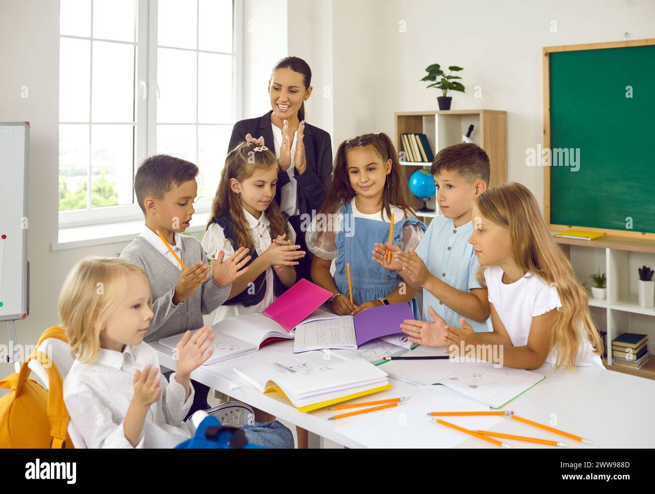 Friendly teacher and group of school students playing in classroom ...