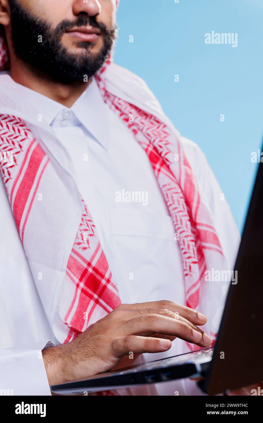 Arab man in thobe and headscarf holding laptop and writing message on ...