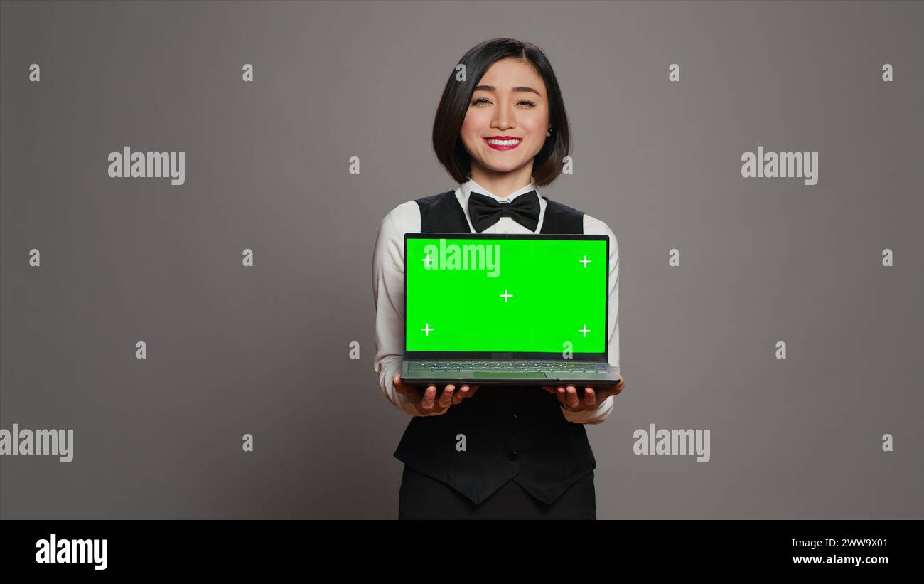 Asian hotel concierge holding pc with greenscreen on camera, presenting ...
