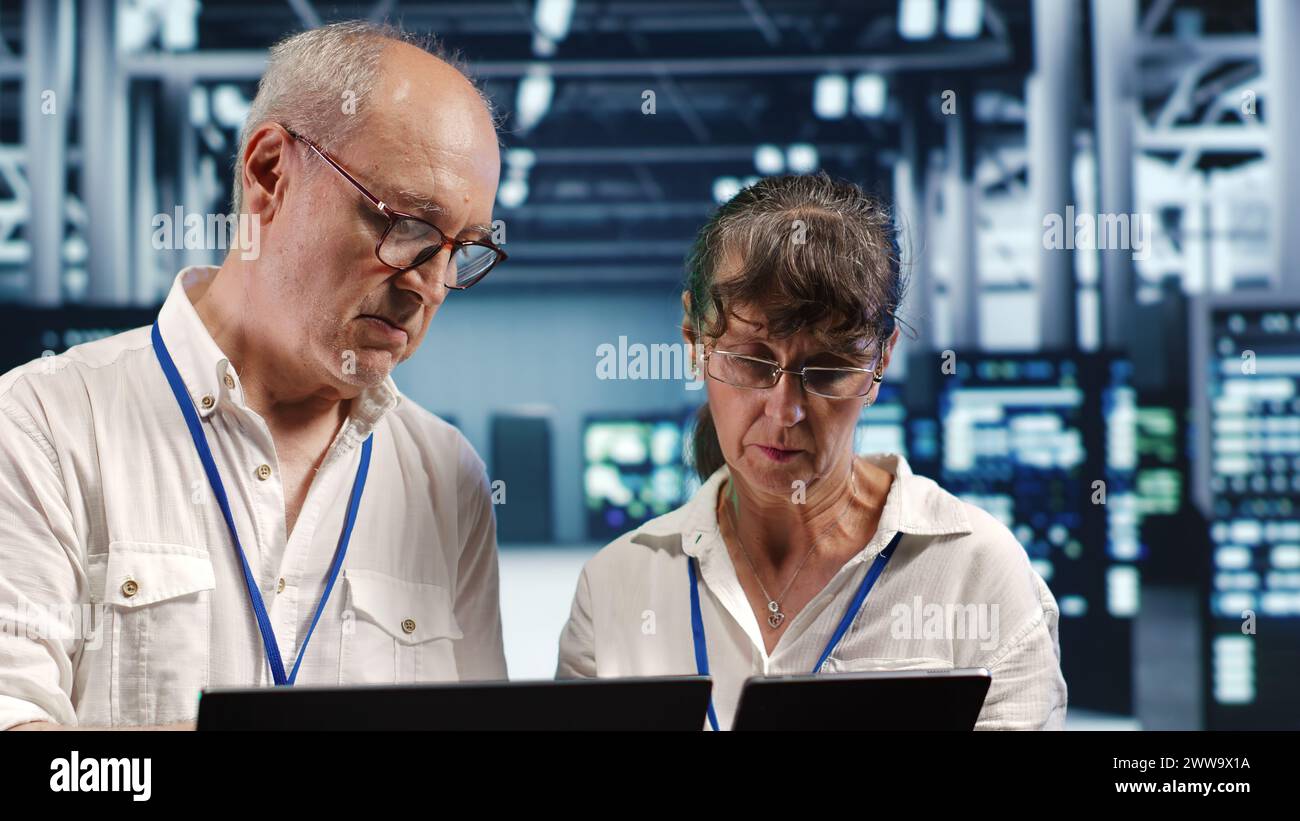 Coworkers looking around high tech data center, using laptop and tablet to crosscheck disaster ...