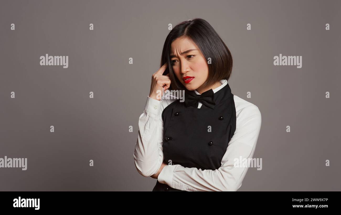 Restaurant hostess being thoughtful over grey background, thinking ...