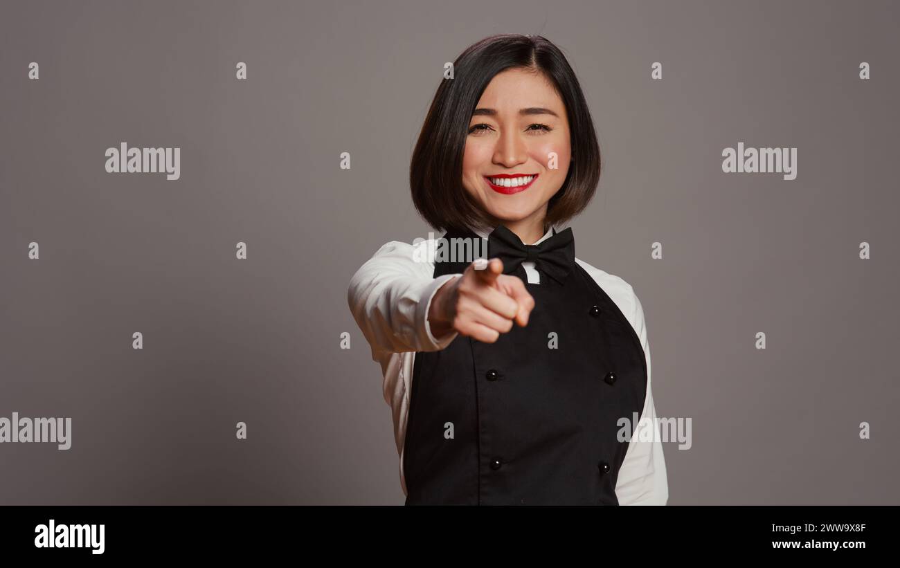 Asian waitress pointing at camera to choose you over grey background ...