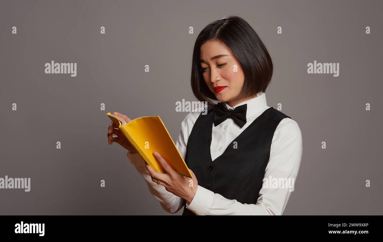 Asian receptionist reading a literature book over grey background ...