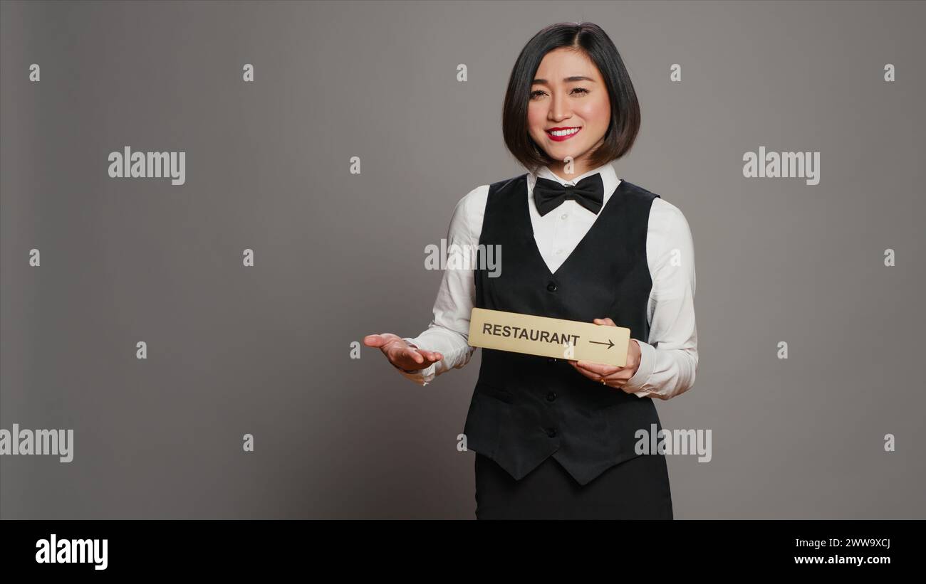 Asian hotel concierge holding restaurant sign to indicate direction ...