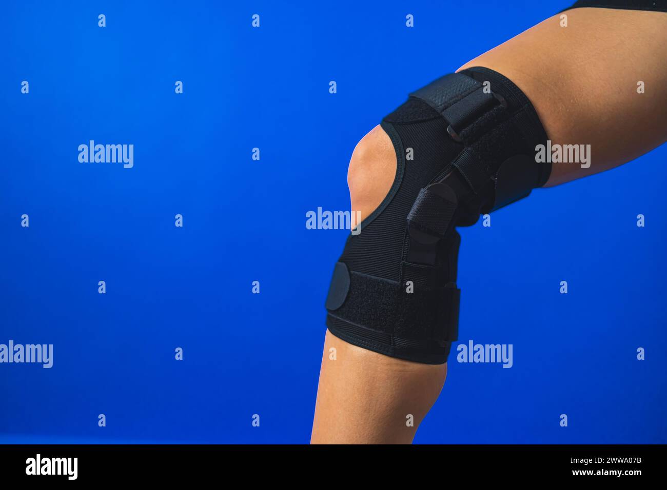 woman adjusting a knee support brace, closeup shot blue background ...