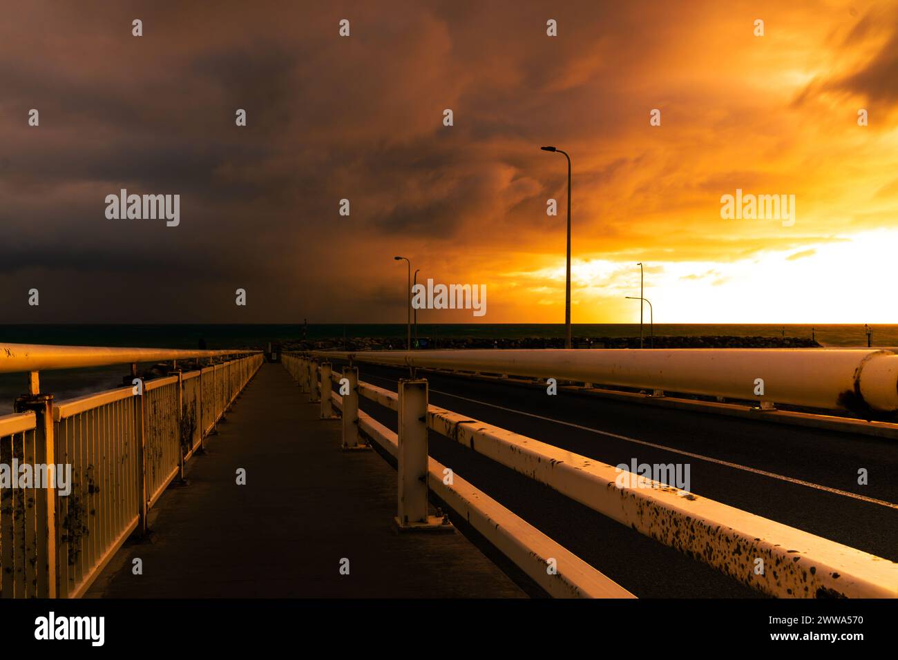 The dark silhouette of a bridge against a fiery sunset over a quiet ...