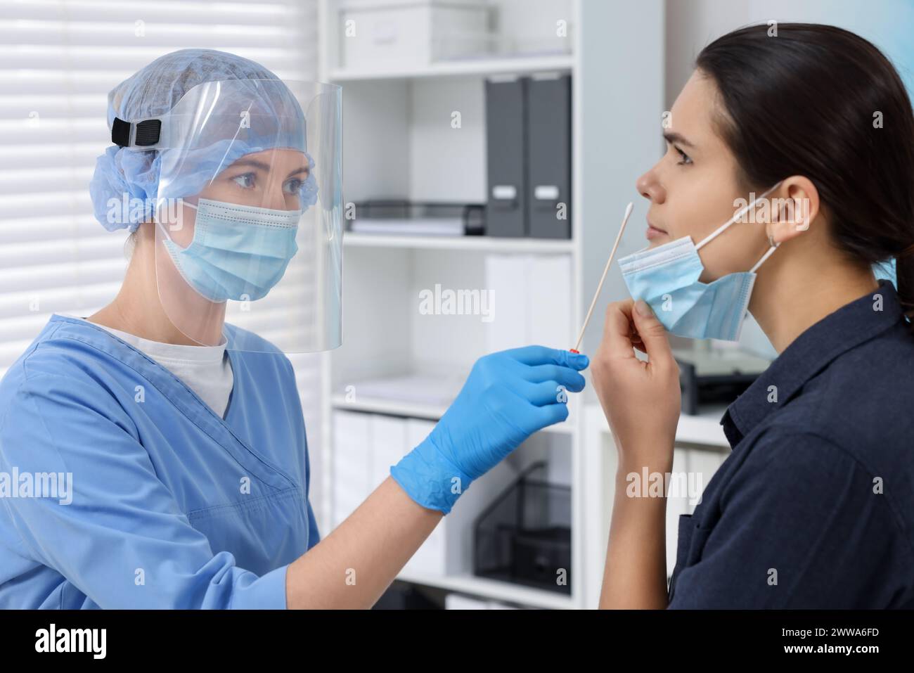 Laboratory testing. Doctor in uniform taking sample from patient's nose ...