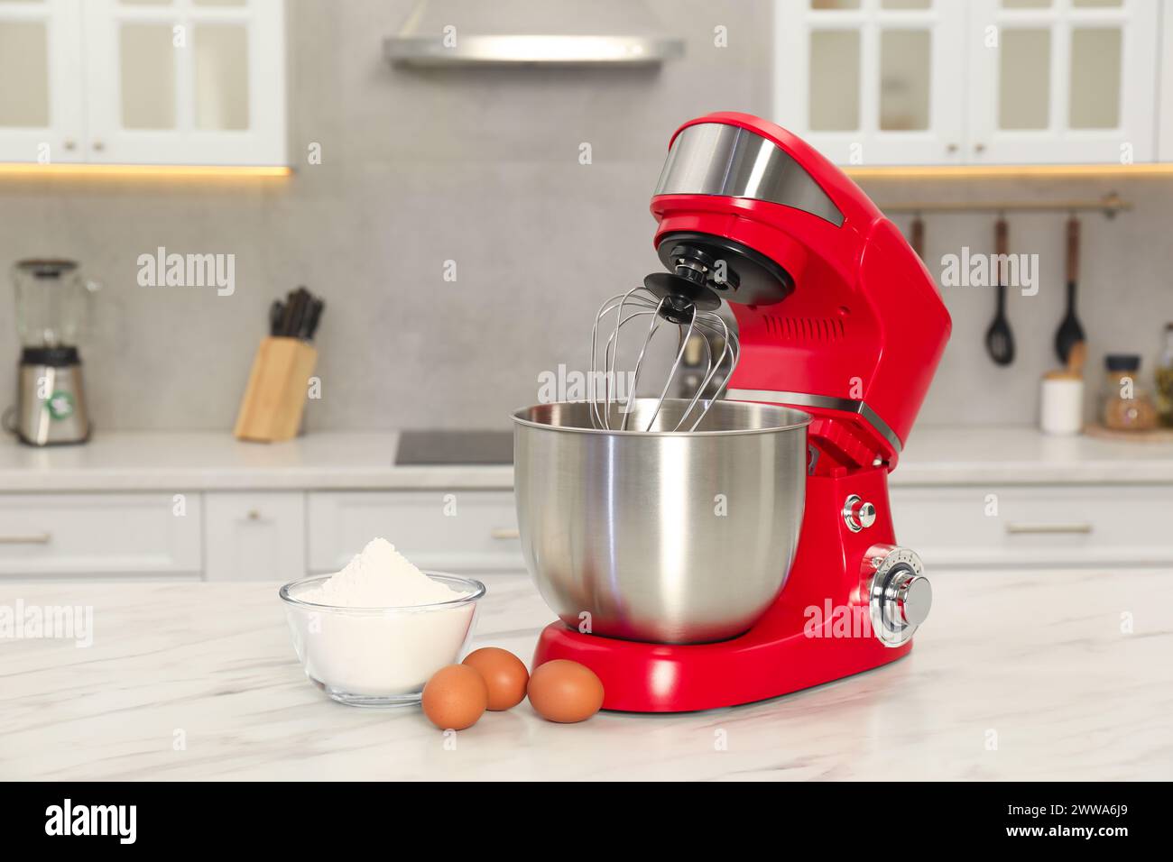 Modern red stand mixer, eggs and bowl with flour on white marble table ...