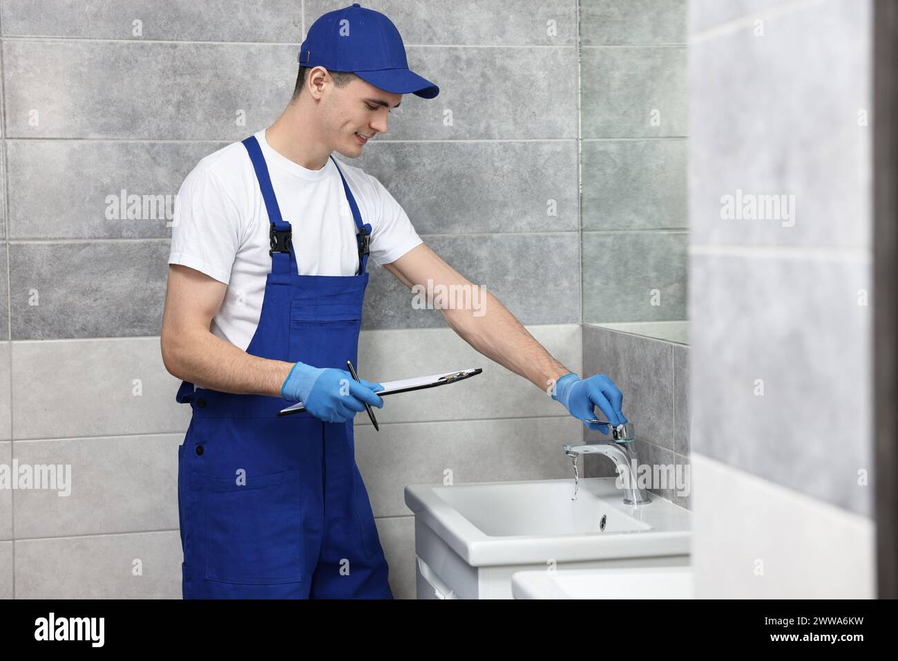 Smiling plumber with clipboard examining faucet in bathroom Stock Photo ...