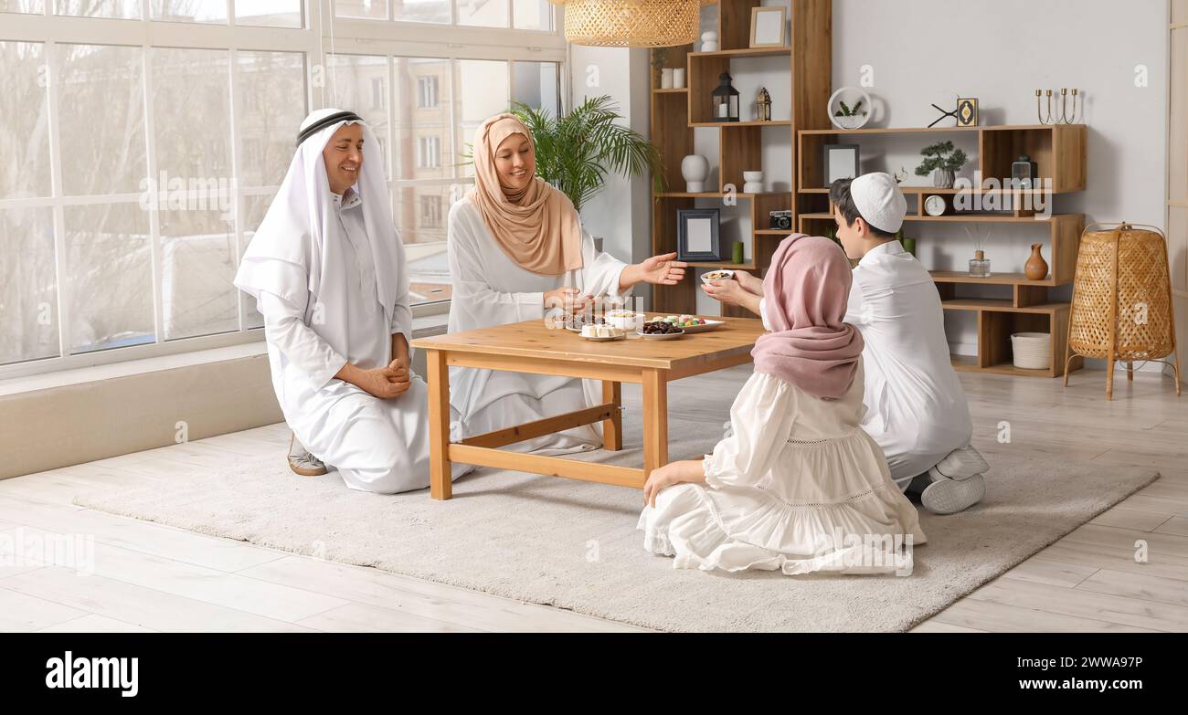 Happy Muslim family eating sweets in living room Stock Photo - Alamy