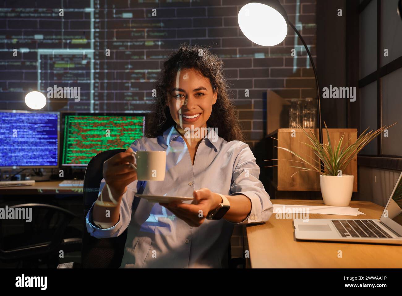 Female African-American programmer with coffee cup in office at night ...