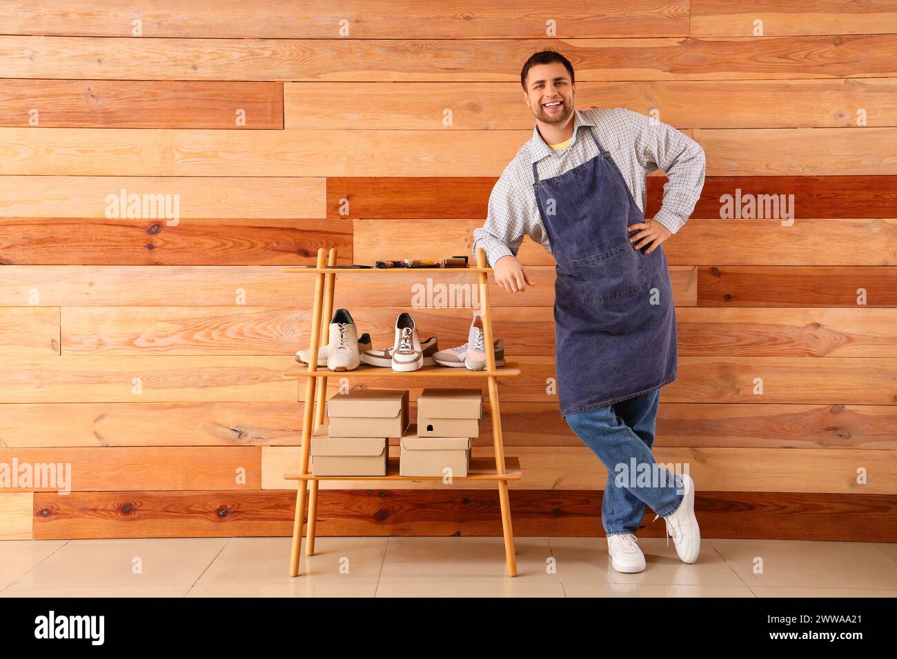 Male shoemaker and shelf unit with shoes near wooden wall Stock Photo ...